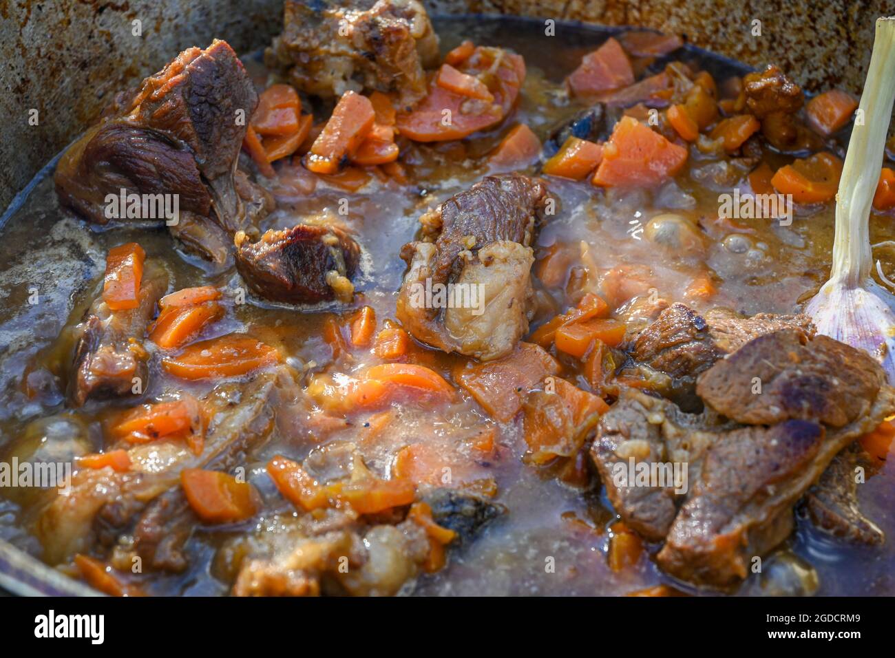 Sliced carrots and pieces of meat in a cauldron in the process of ...