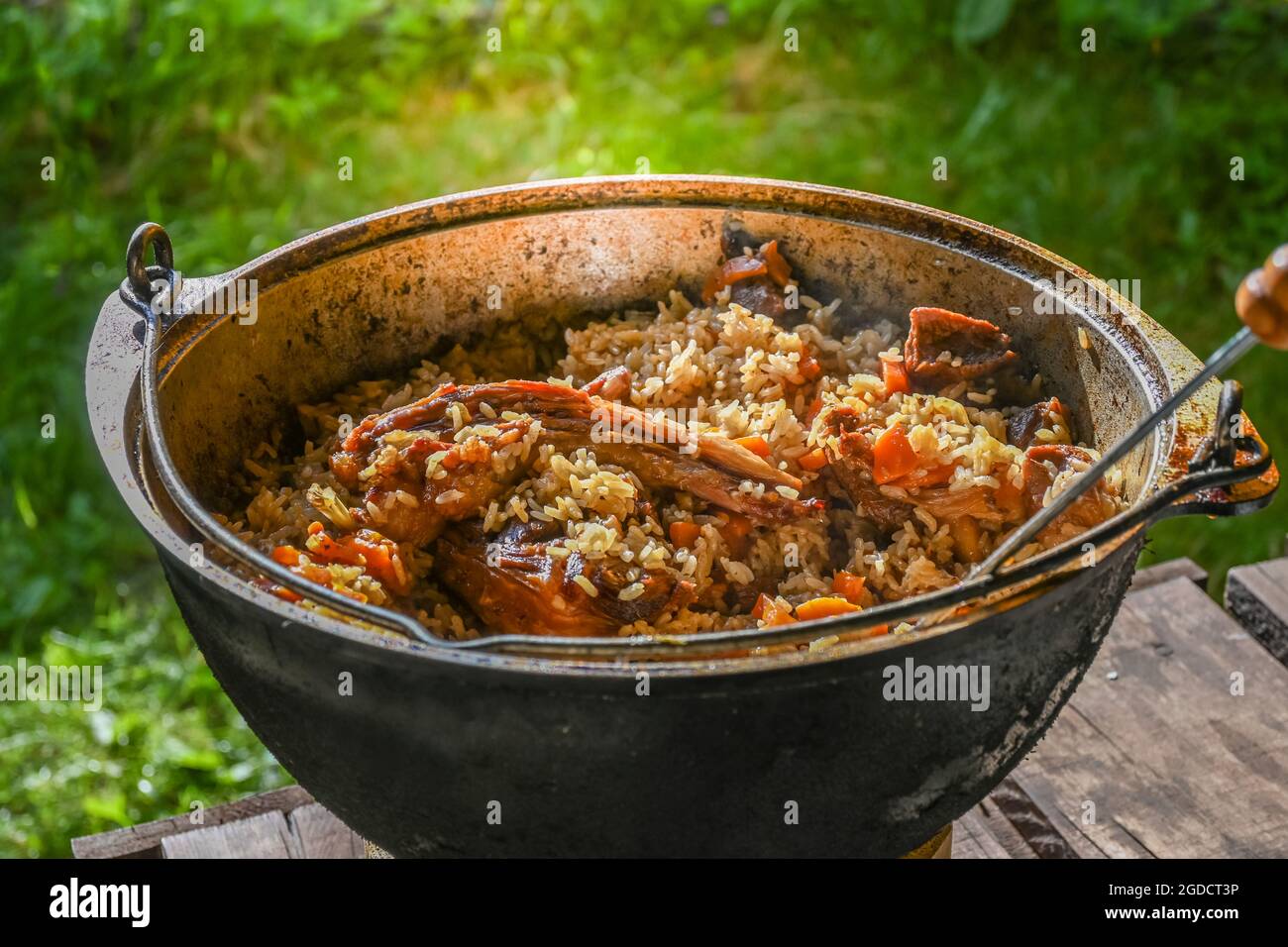 Traditional oriental pilaf in a cauldron on a wooden table on a sunny ...