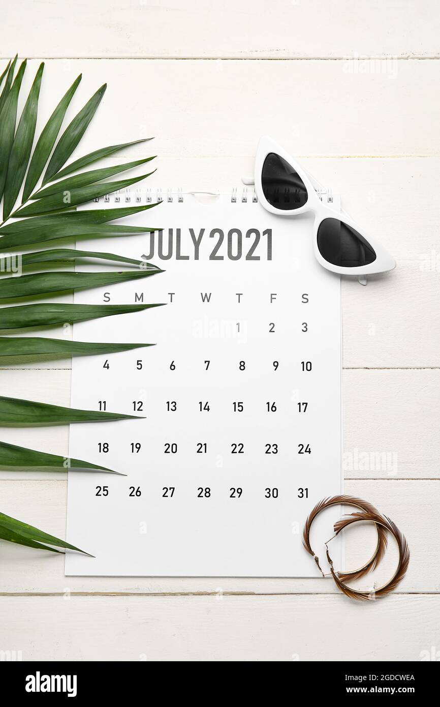 Calendar with female accessories and tropical leaf on light wooden ...