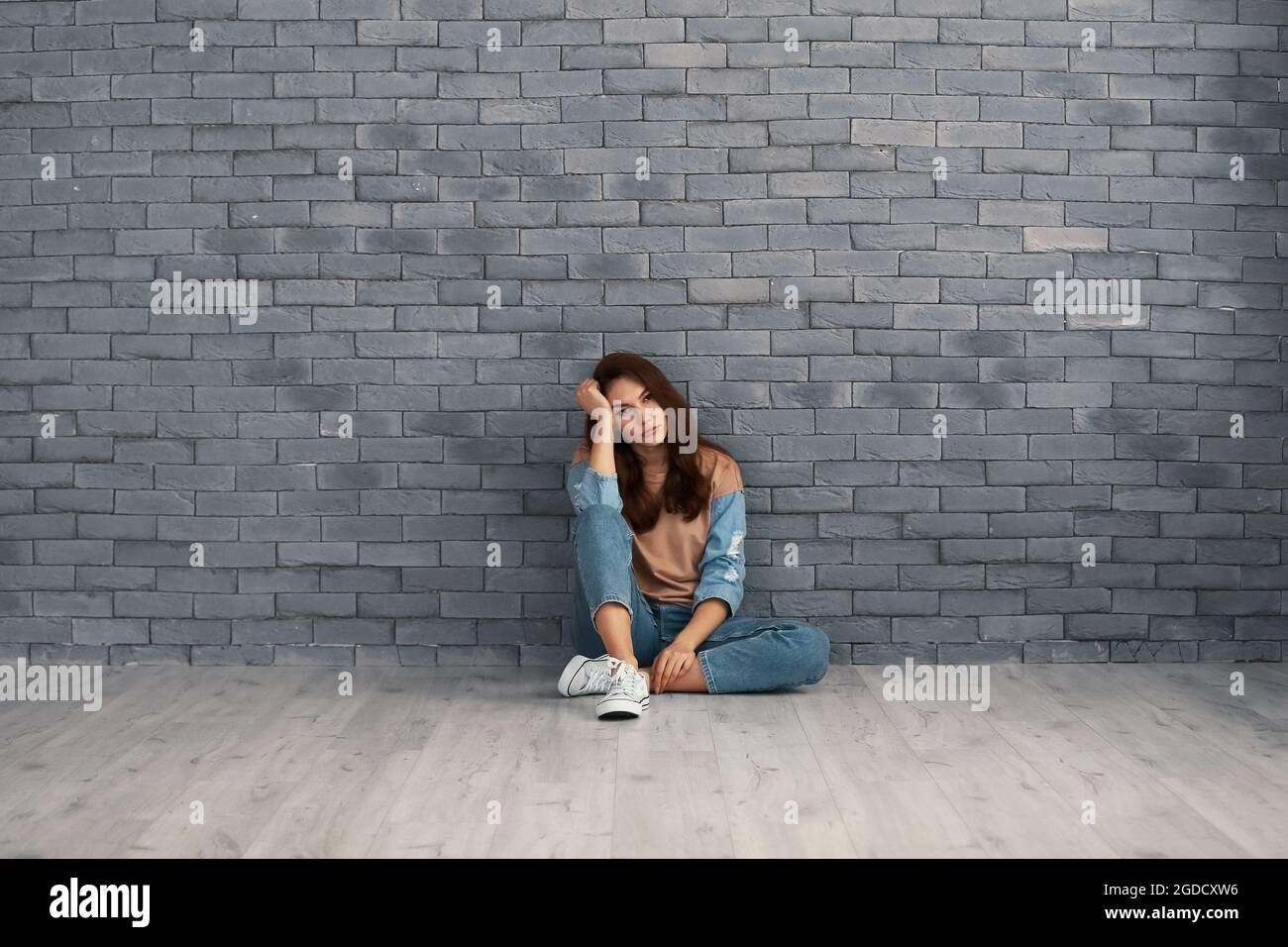 Depressed young woman sitting near brick wall Stock Photo - Alamy