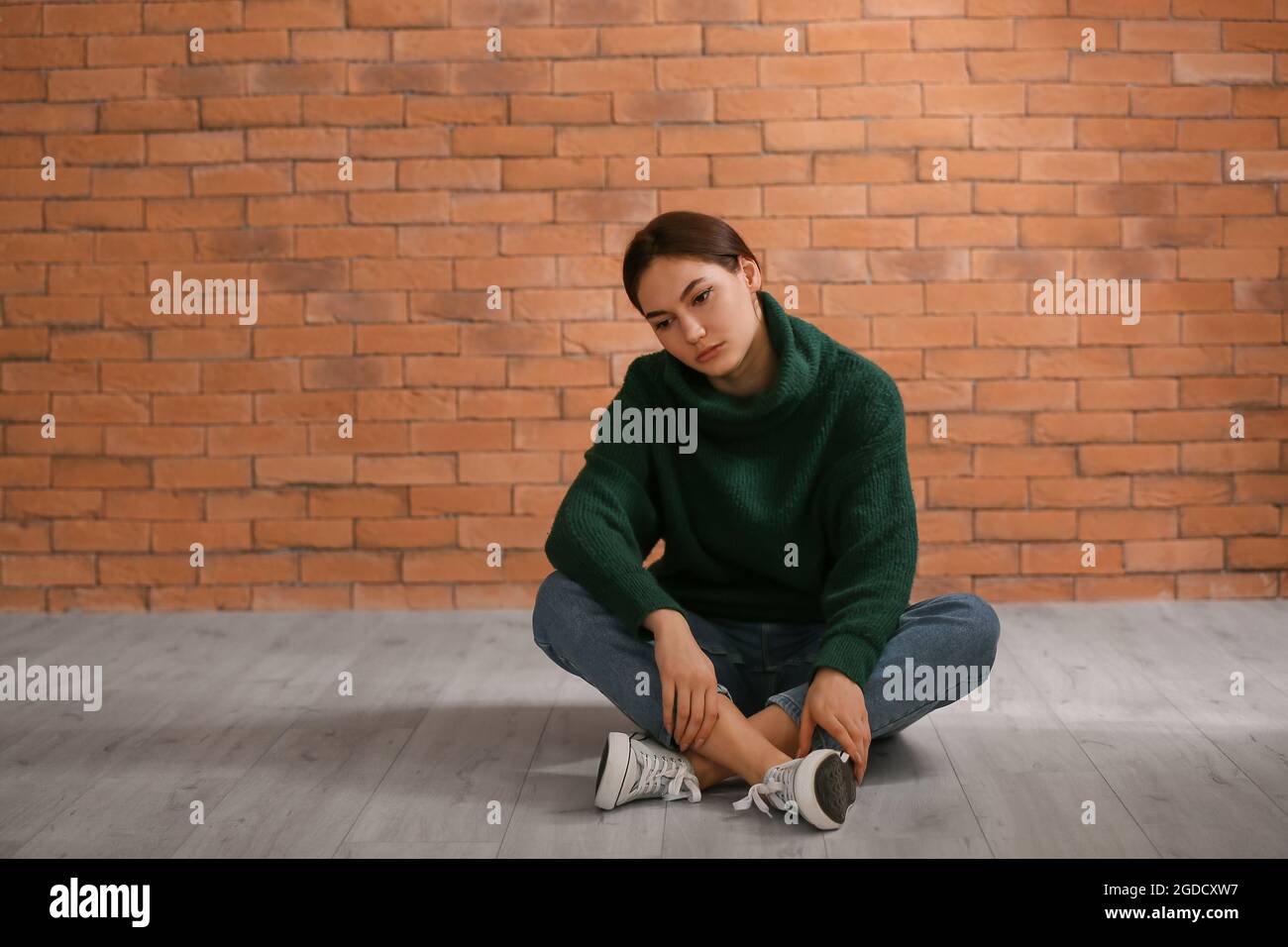 Depressed young woman sitting near brick wall Stock Photo - Alamy