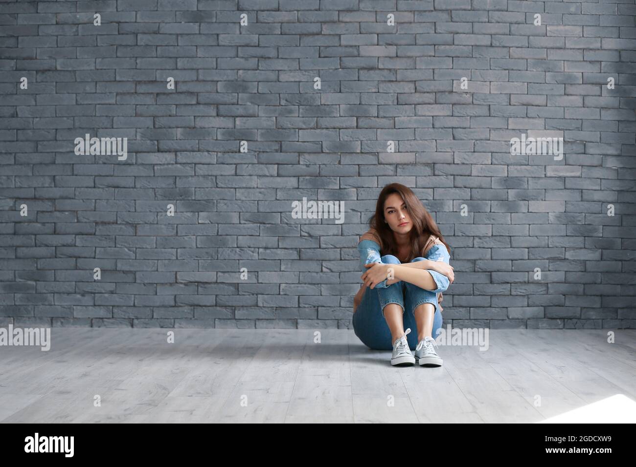 Depressed young woman sitting near brick wall Stock Photo - Alamy