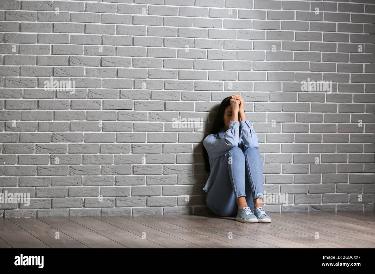 Depressed young woman sitting near brick wall Stock Photo - Alamy