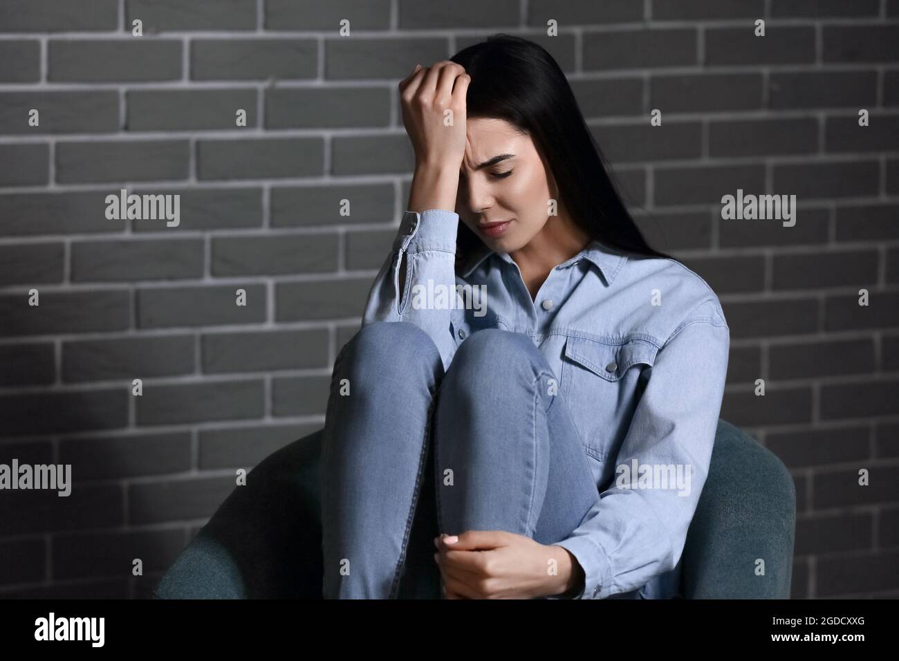 Depressed young woman sitting near brick wall Stock Photo - Alamy