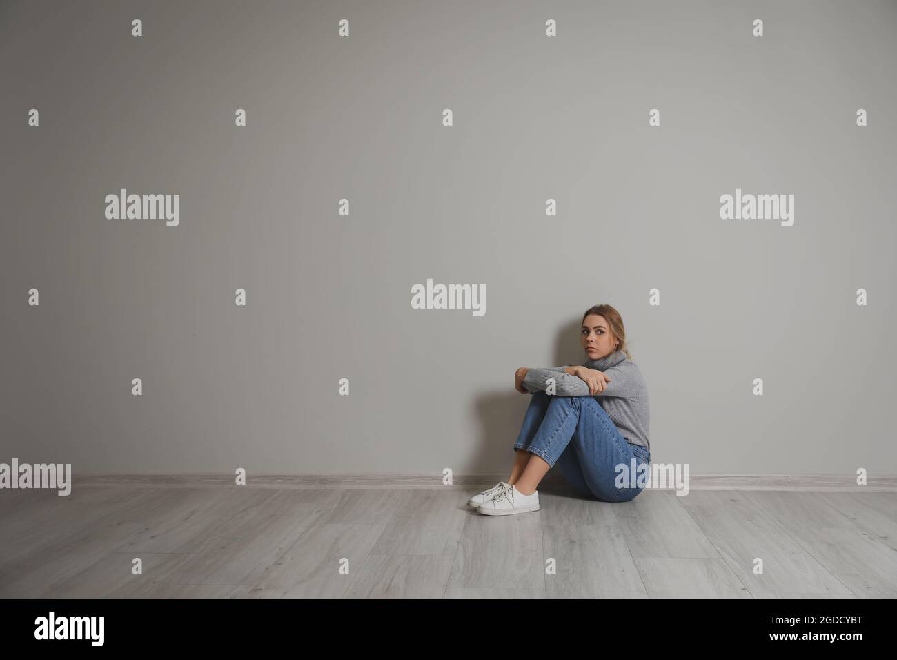 Depressed young woman sitting on floor near grey wall Stock Photo - Alamy