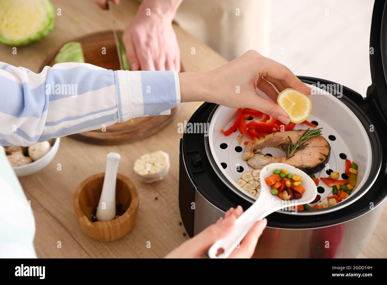 Woman squeezing lemon onto fish in multi cooker Stock Photo - Alamy