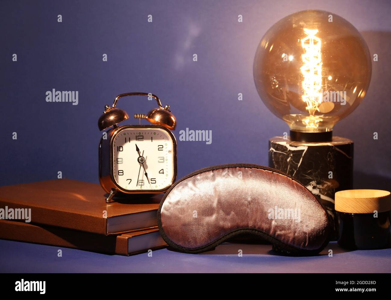 Sleeping mask with alarm clock, books and lamp on color background ...