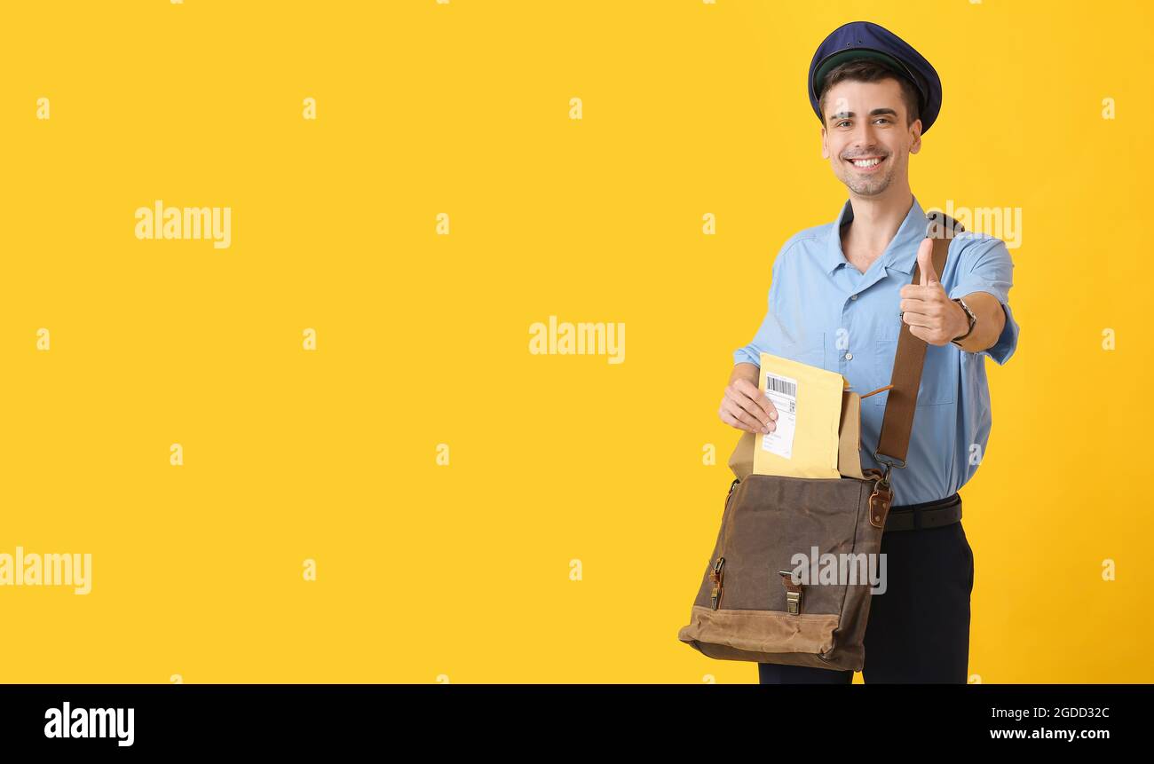 Handsome young postman showing thumb-up on color background Stock Photo ...