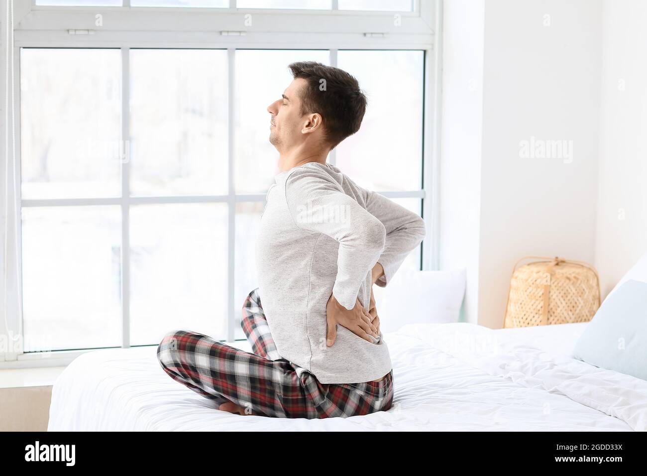 Young man suffering from back pain in bedroom Stock Photo - Alamy