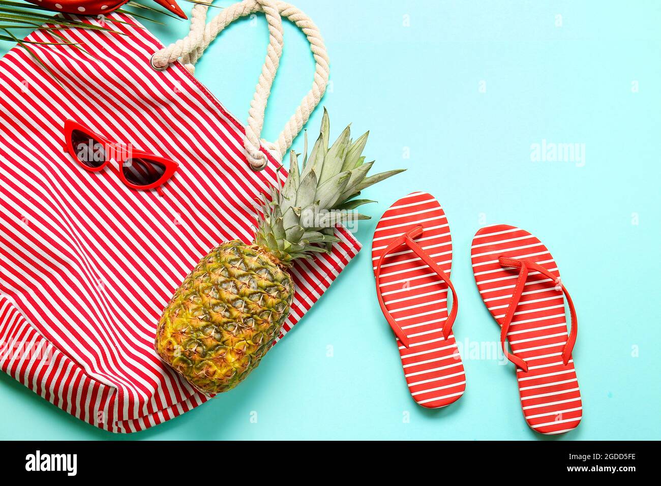 Stylish sunglasses, bag, flip-flops and pineapple on color background ...