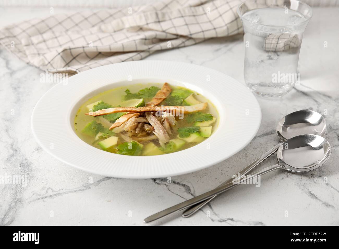 Plate with tasty Sopa de Lima soup and glass of water on light ...