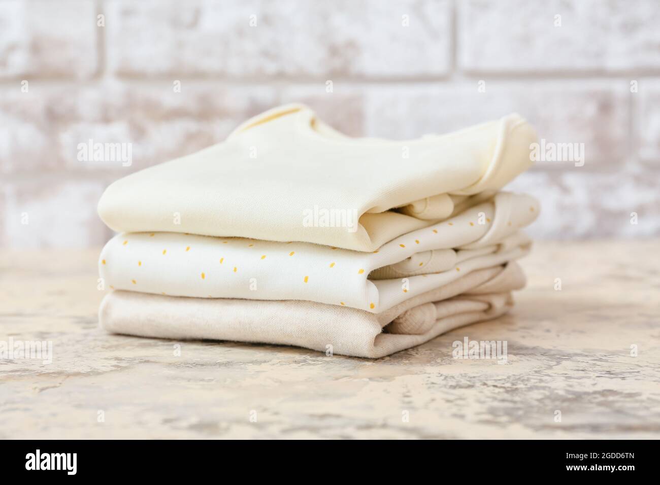 Stack of baby clothes on table against brick wall Stock Photo - Alamy
