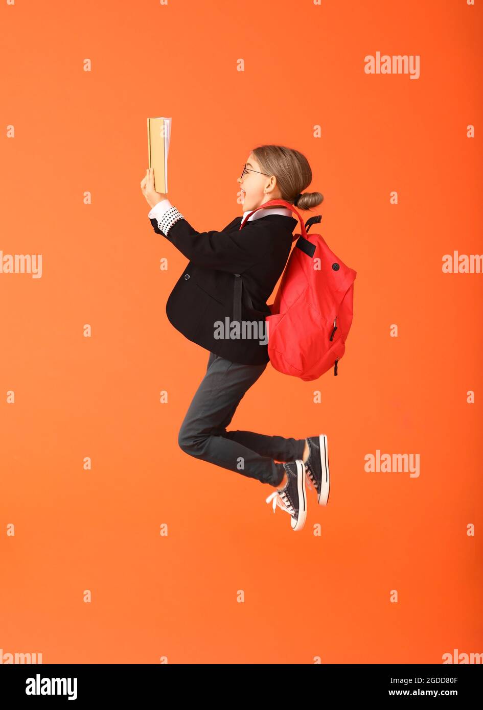 Jumping little school girl with book on color background Stock Photo ...