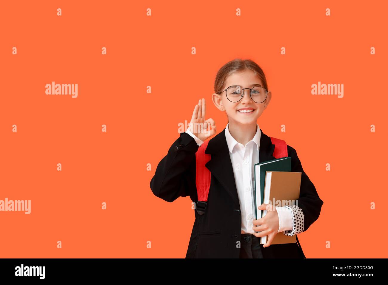 Cute little school girl with books showing OK gesture on color ...