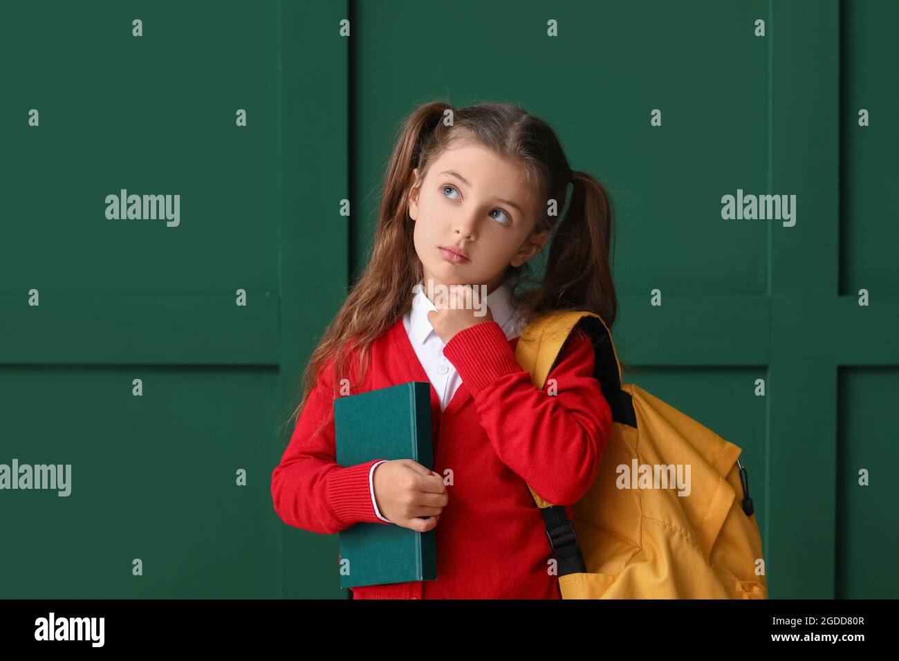 Thoughtful little school girl with book on color background Stock Photo ...