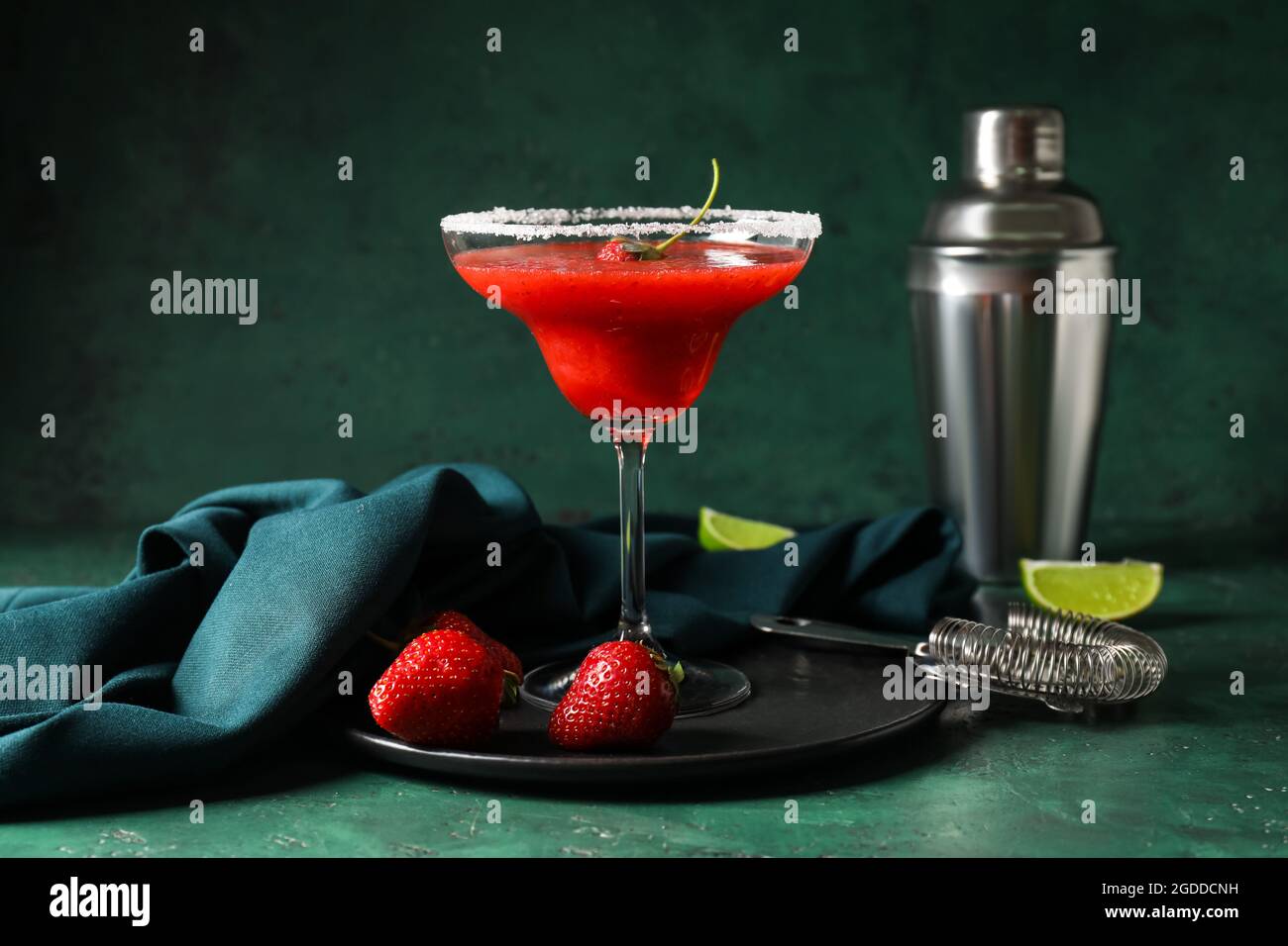 Glass of strawberry daiquiri cocktail, shaker and strainer on color ...