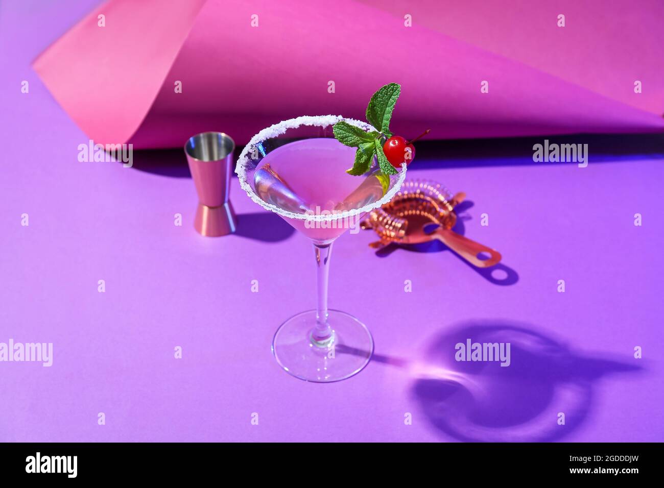 Glass of tasty cosmopolitan cocktail, shaker and strainer on color ...