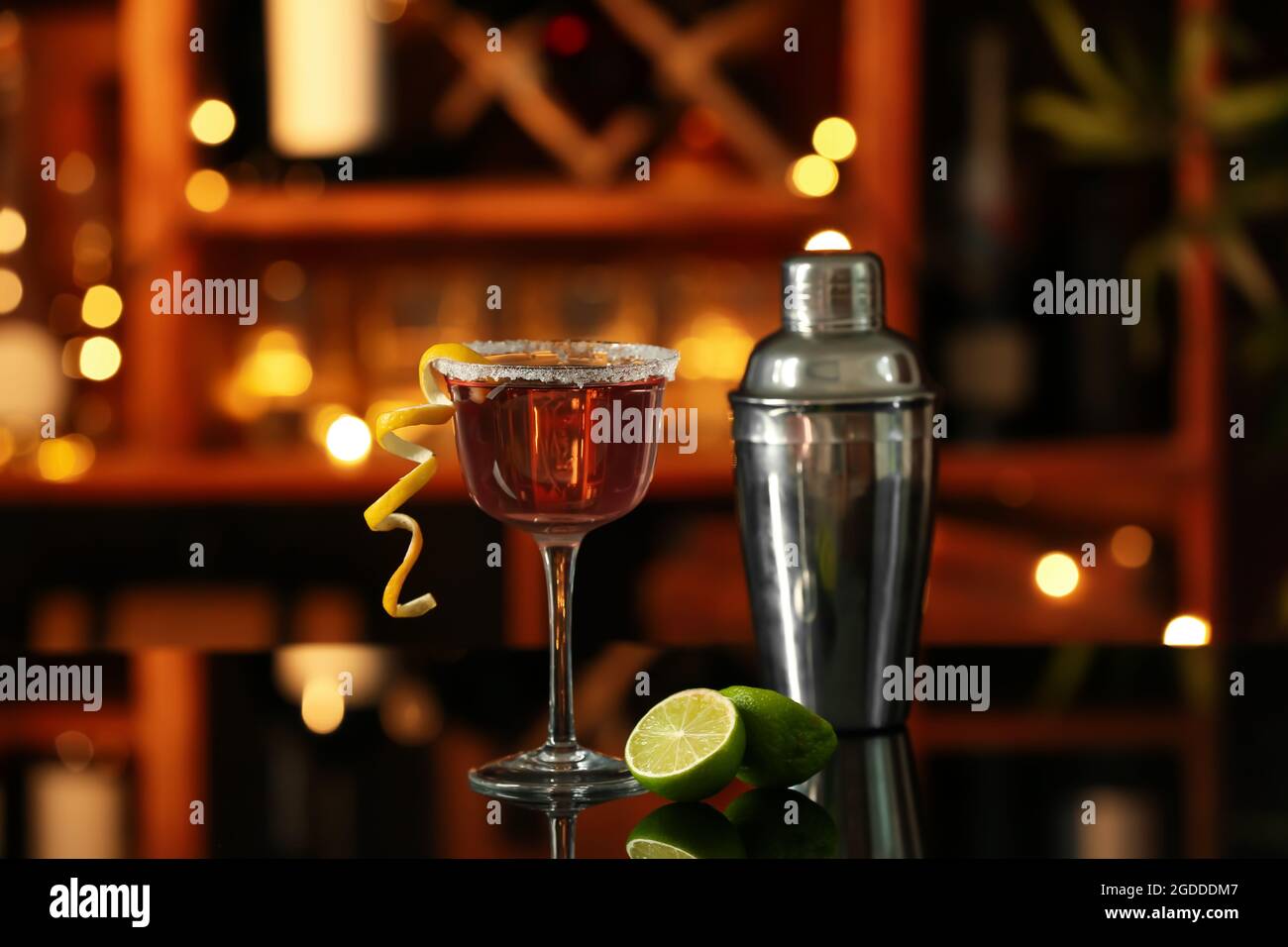 Glass of tasty cosmopolitan cocktail, shaker and lime on table in bar ...
