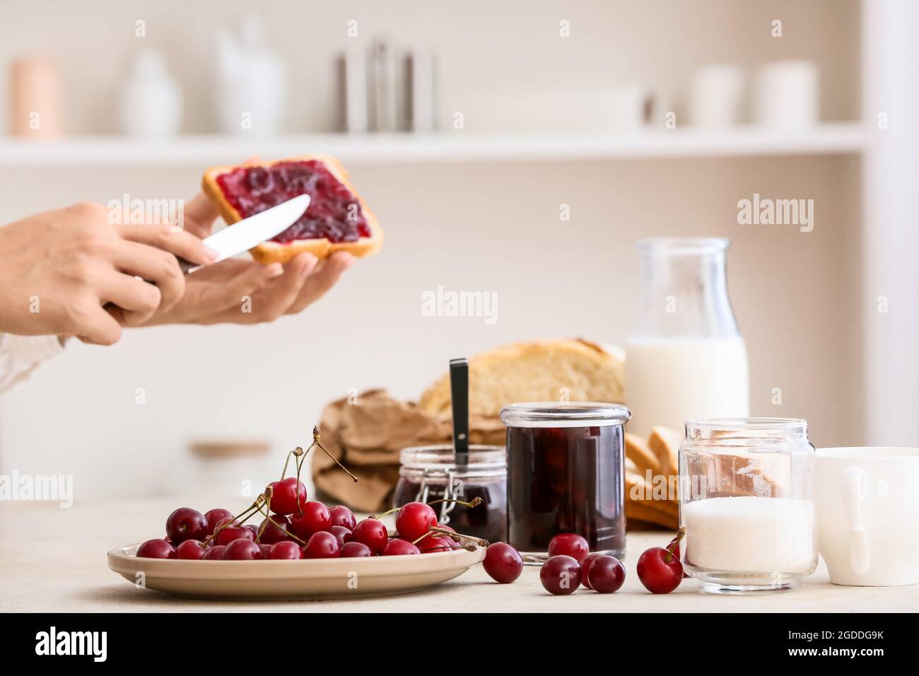 Woman spreading tasty cherry jam onto bread in kitchen Stock Photo - Alamy