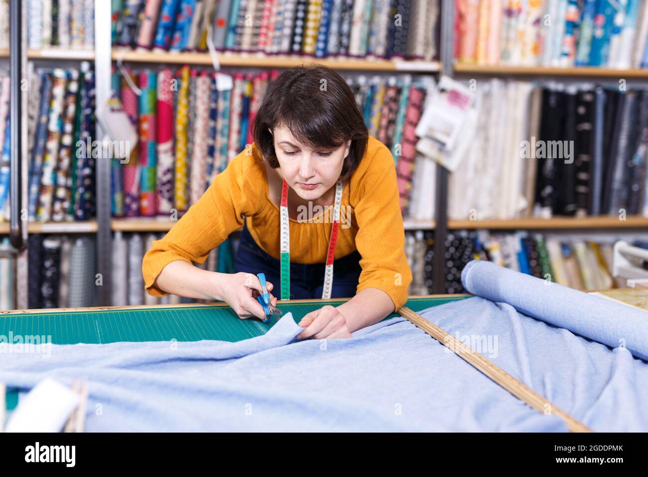 Saleswoman measuring and cutting off piece of cloth Stock Photo - Alamy