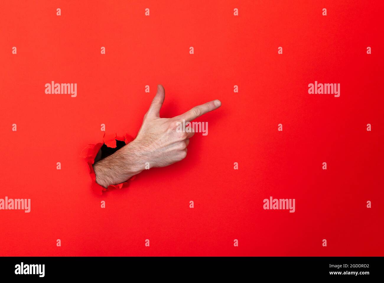 Male caucasian hand through a hole pointing against a red background ...