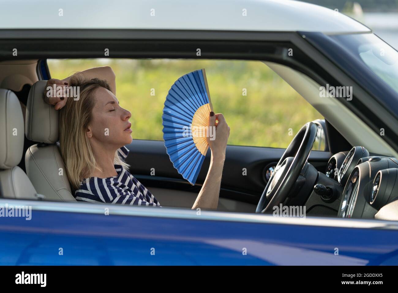Female driver with hand fan suffering from heat in car, has problem ...