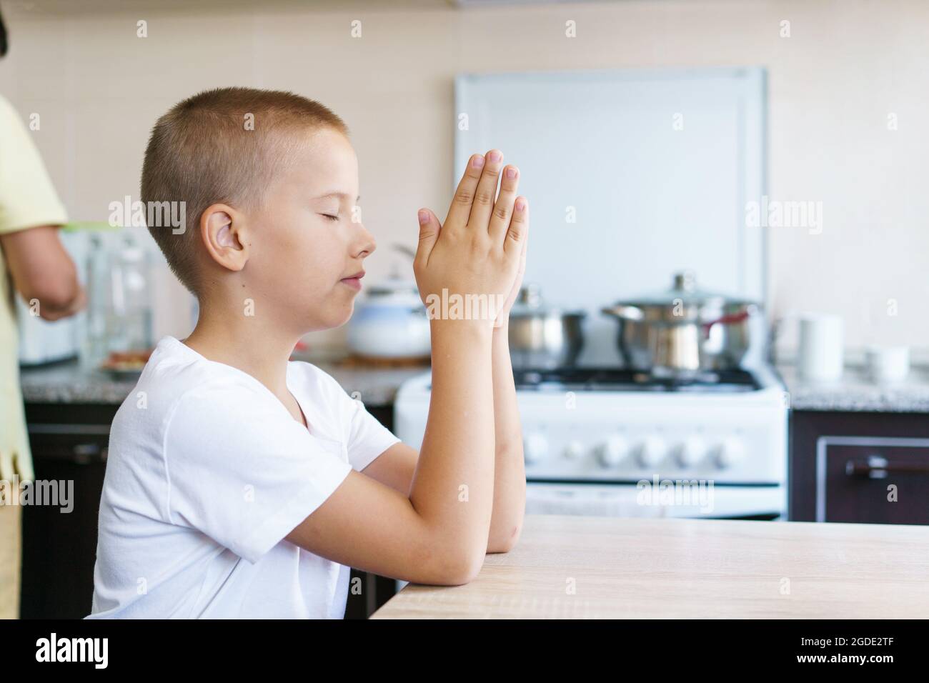 Caucasian boy prays at home at the table before eating. Stay home and ...
