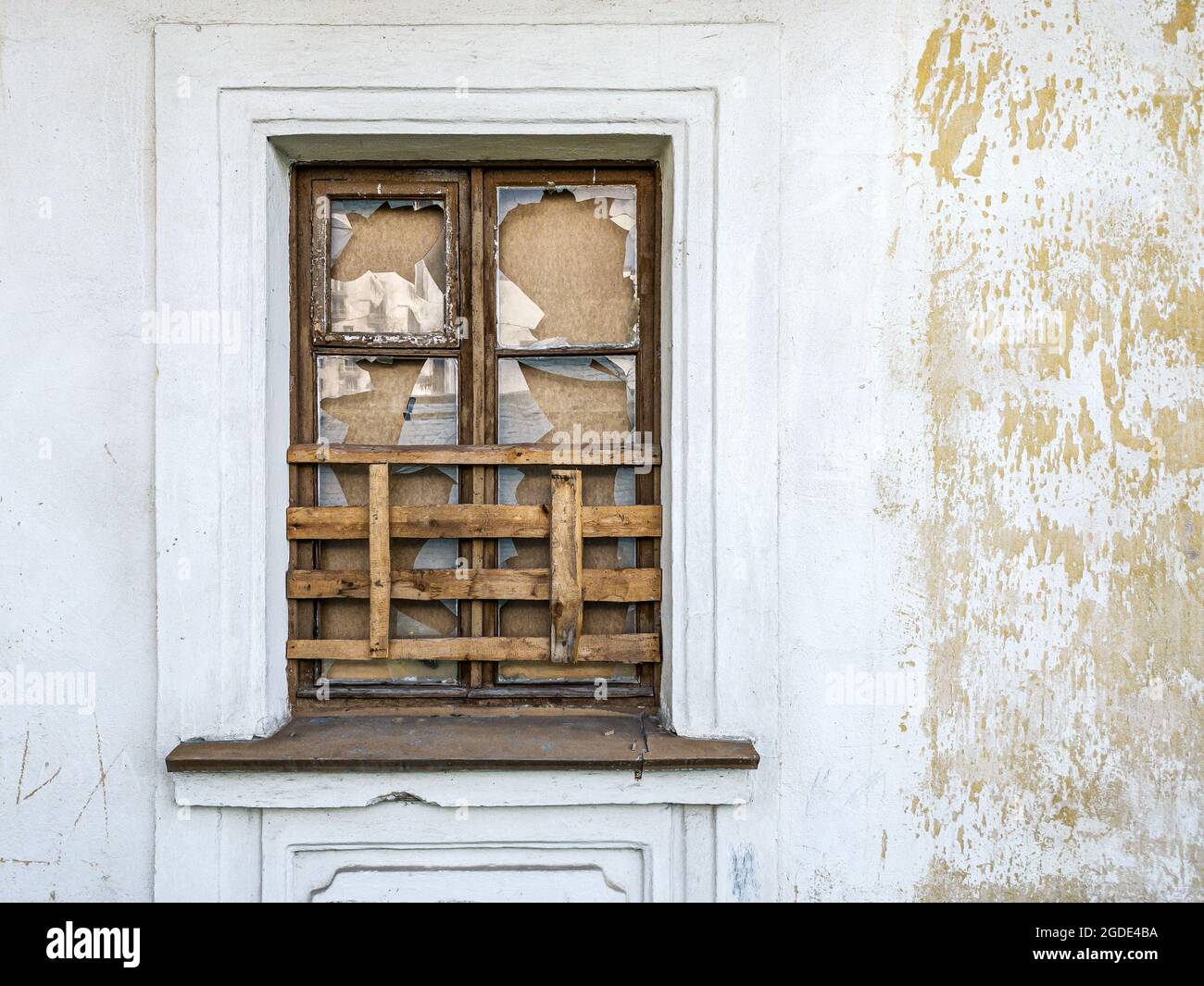 boarded up window with broken glass on weathered plaster wall of ...
