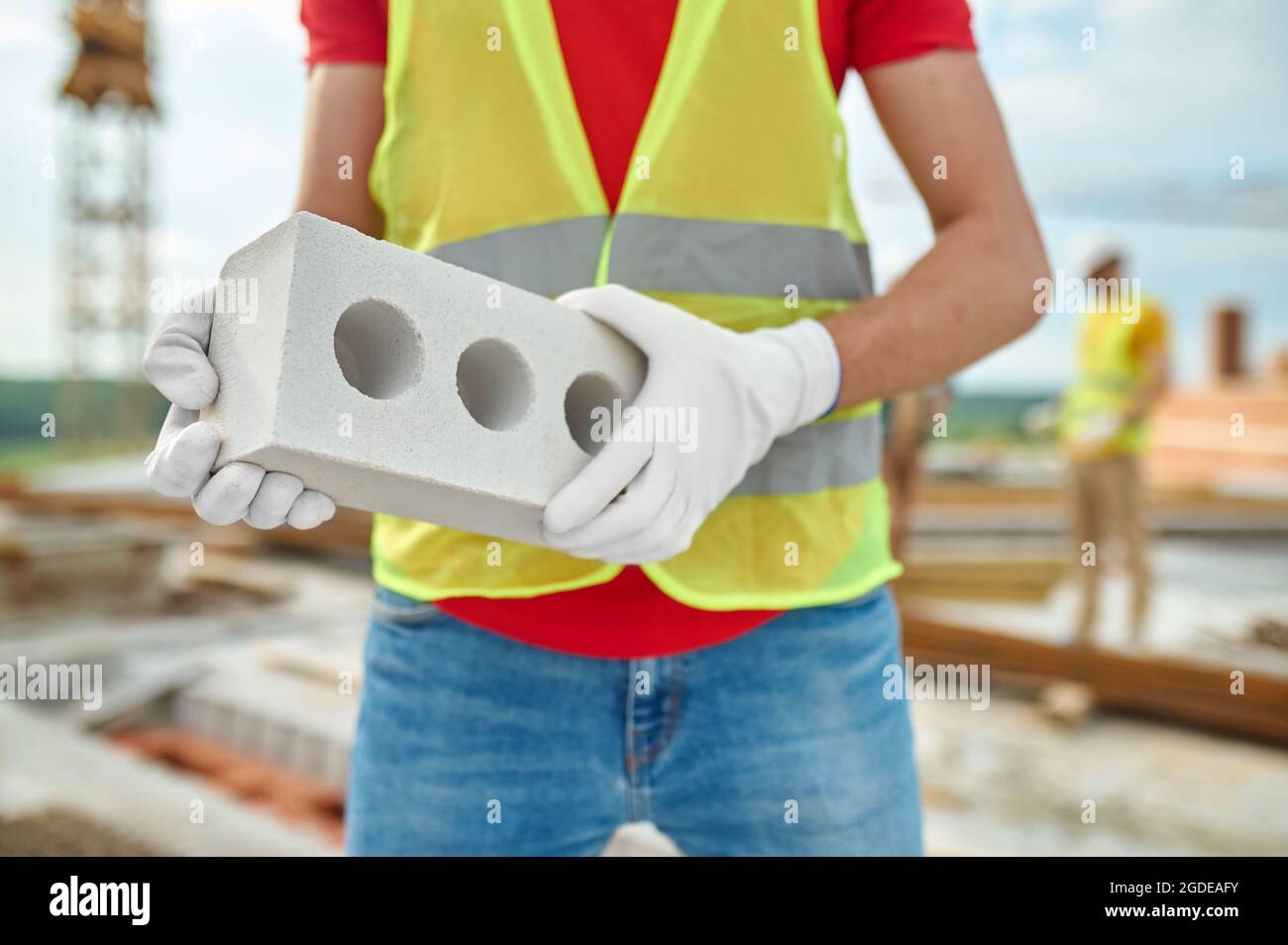 Bricklayer in cotton gloves and a protective vest standing outdoors ...