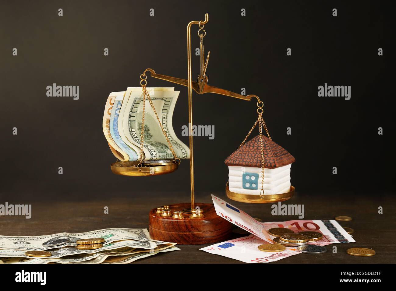 Scale with money and model of house on dark background Stock Photo - Alamy