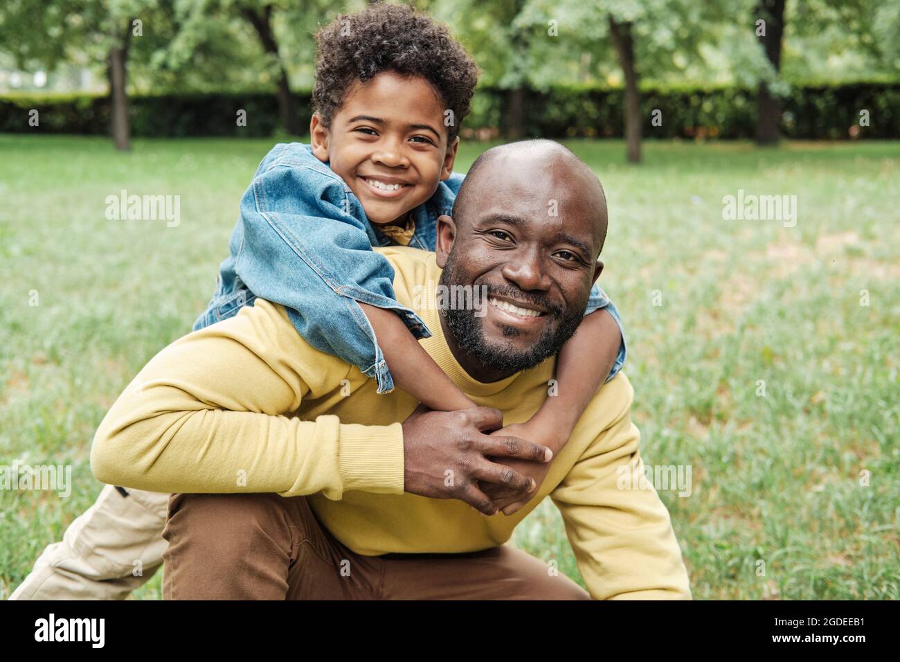 Portrait of happy African father smiling at camera while carrying his ...