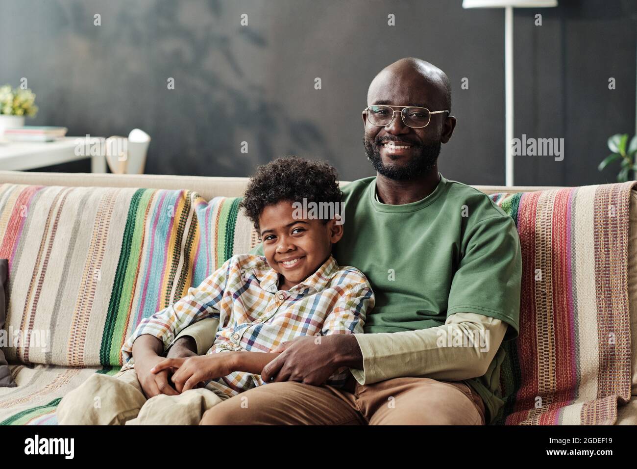 Portrait of happy African father embracing his little son while they ...