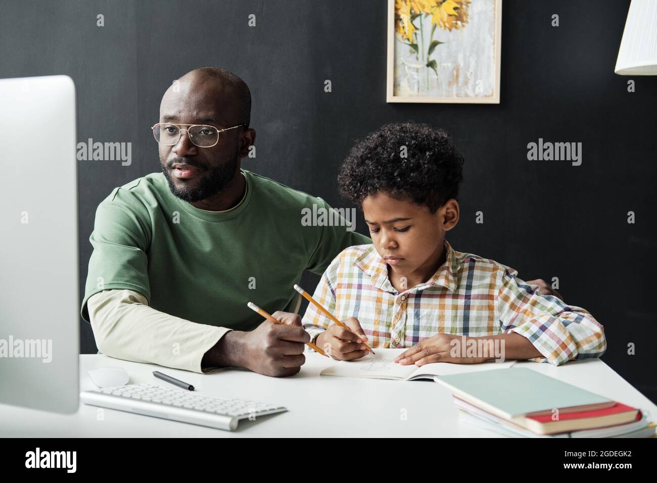 African father helping his son in study while they sitting at the table ...