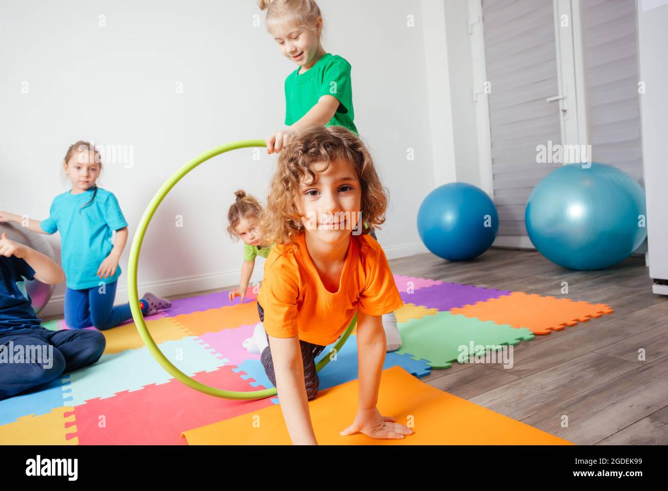 Curly girl crawling on colorful floor through hula hoops Stock Photo ...