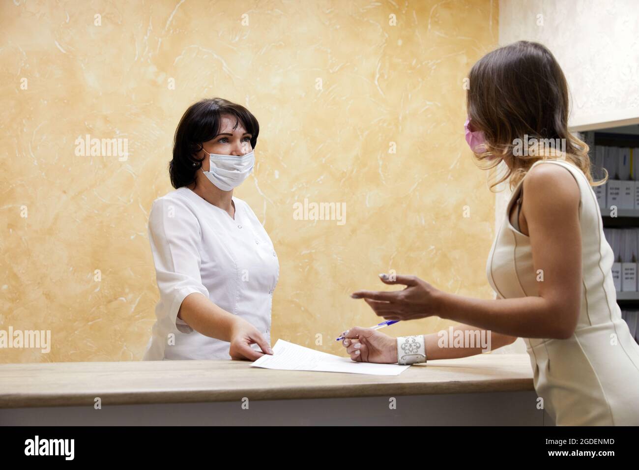 Client Signing Paper At Reception Desk In Face Mask Stock Photo - Alamy