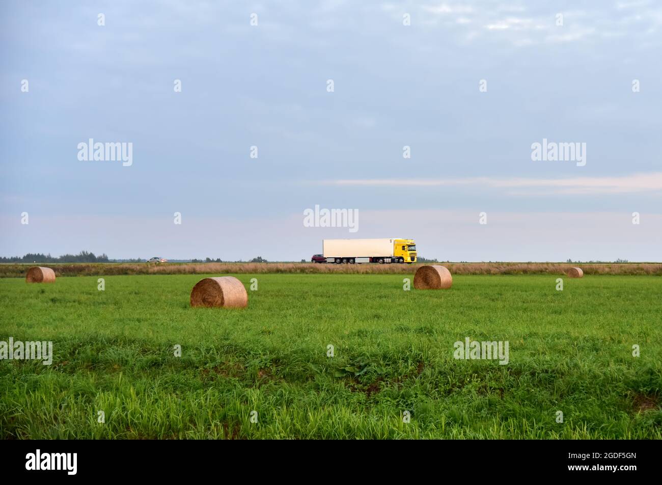 View of a field with hay in rolls against the background of trucks with ...