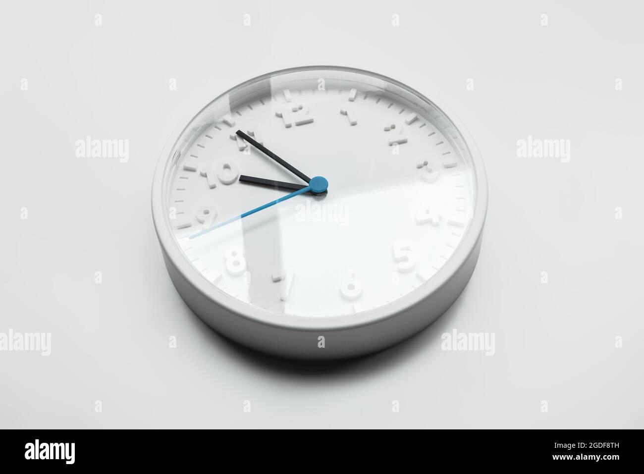 A Modern white wall clock in sunlight with shadows on the clock face ...