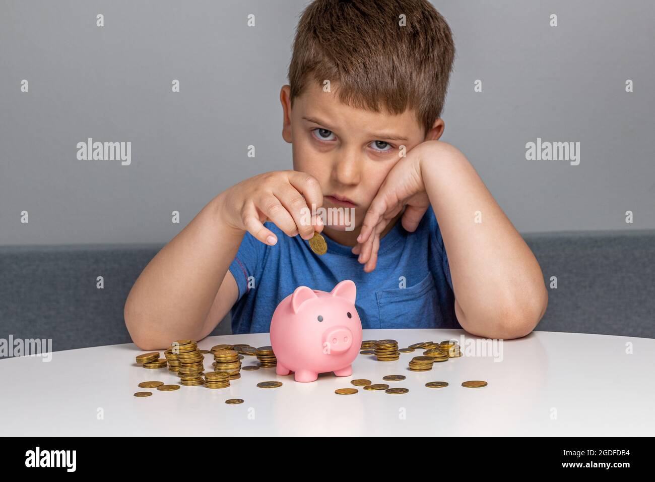 Sad boy lays down a coin in the piggy bank Stock Photo - Alamy