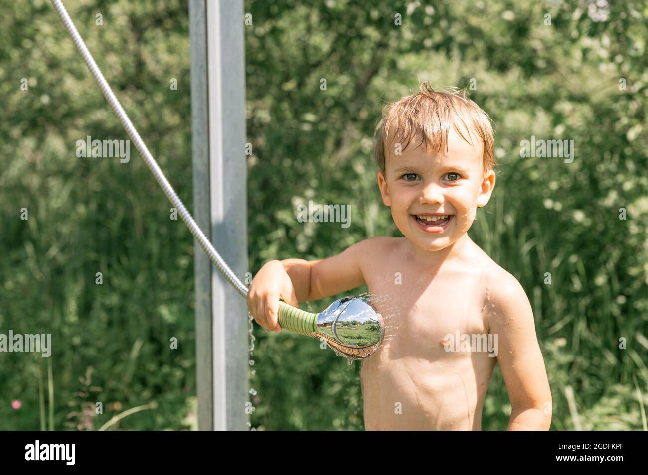 little four year old kid boy fun pours himself with cold water from a ...