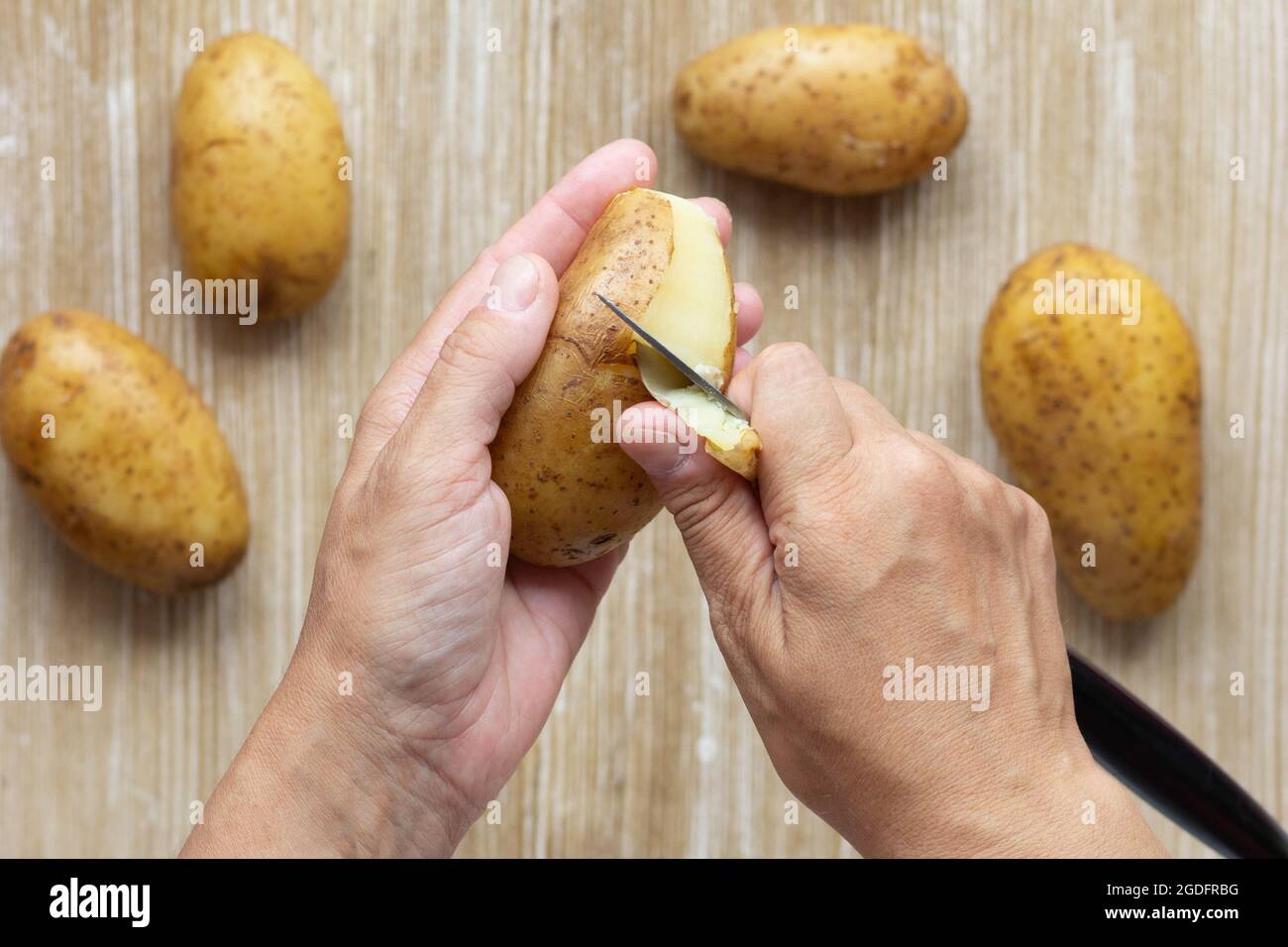Top view of woman hands scrubbing boiled potato in jacket using knife ...