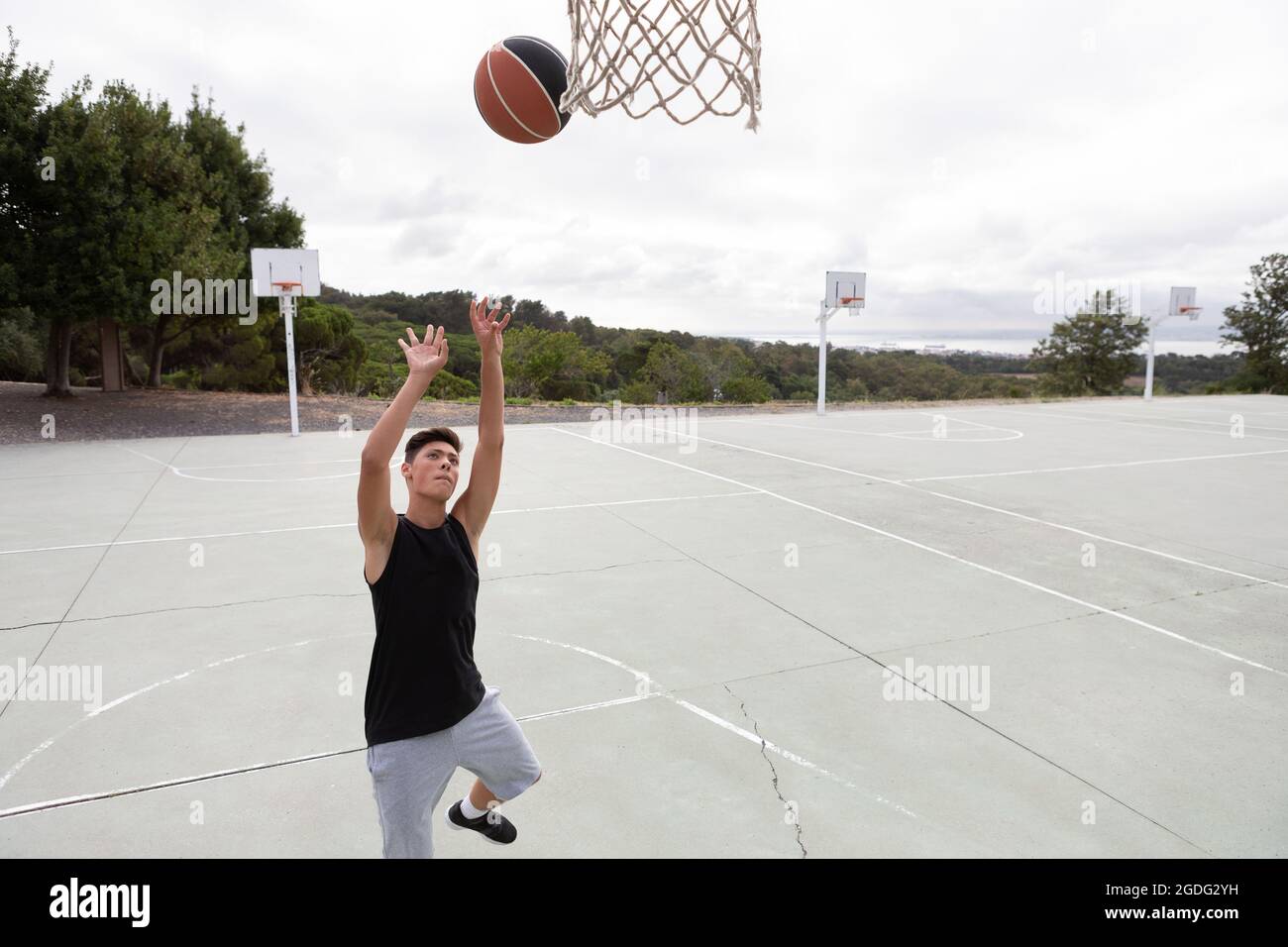 Male teenage basketball player throwing ball toward basketball hoop ...