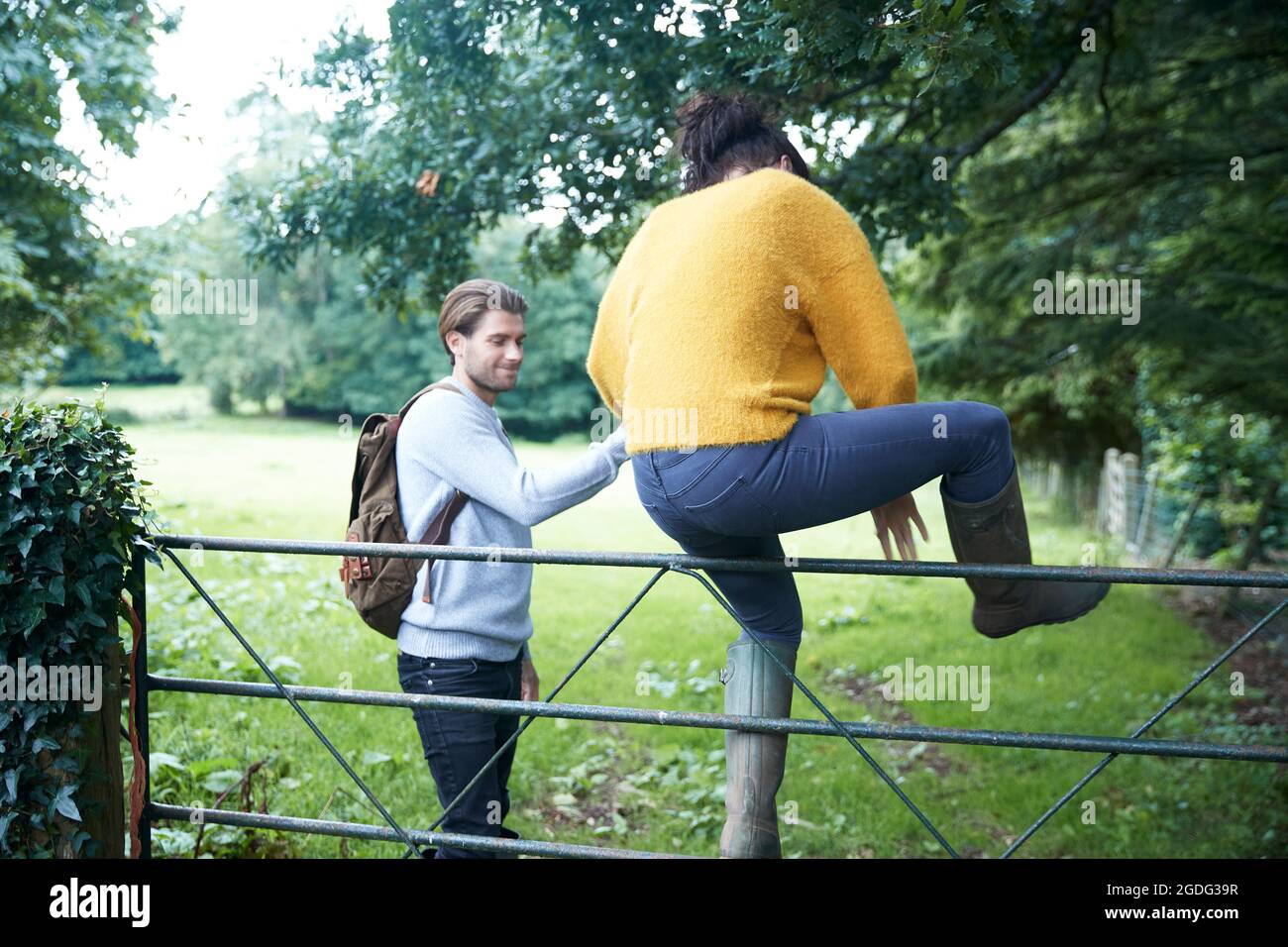 Hiker couple climbing over farm gate Stock Photo - Alamy