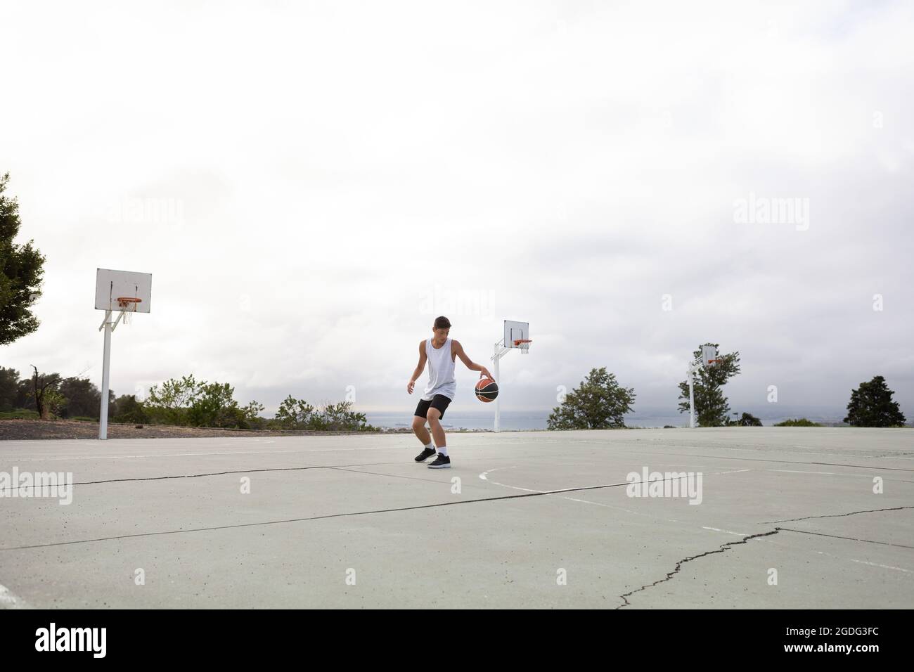Male teenage basketball player practicing with ball on basketball court ...