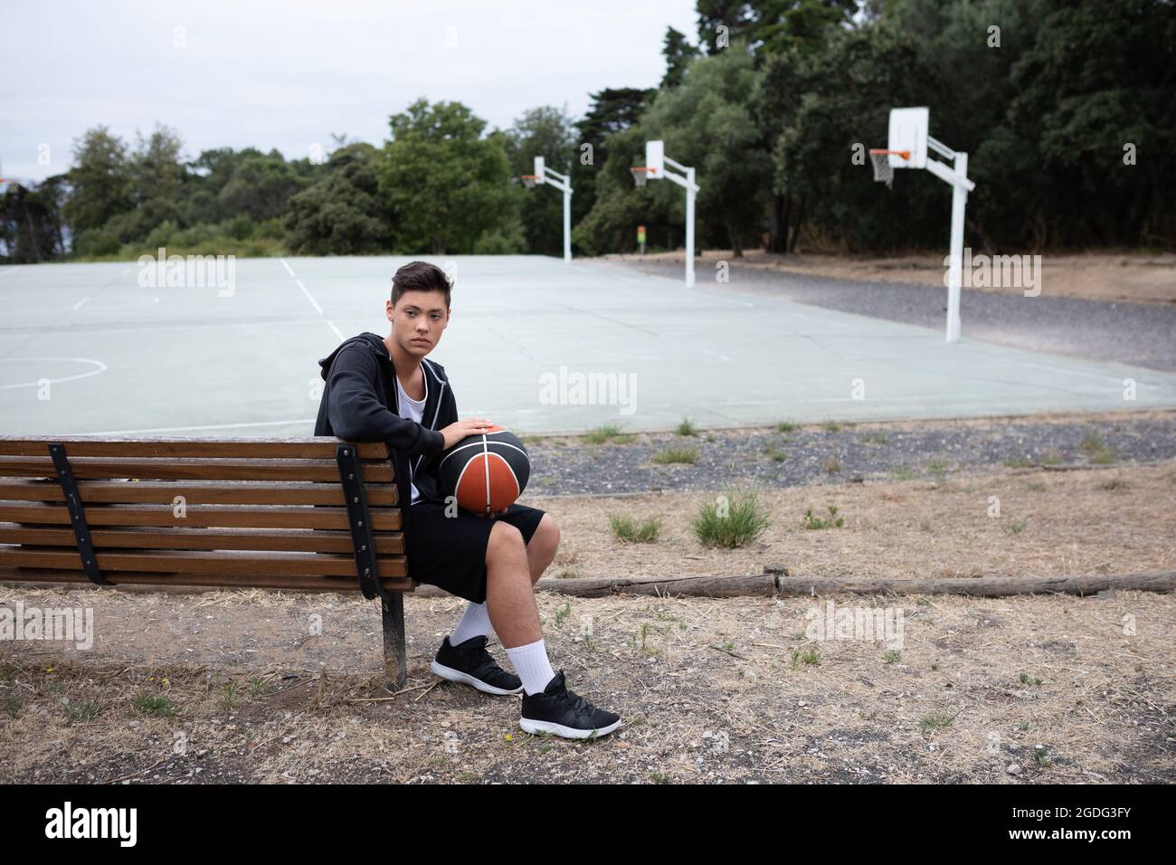 Male teenage basketball player sitting on park bench by basketball ...