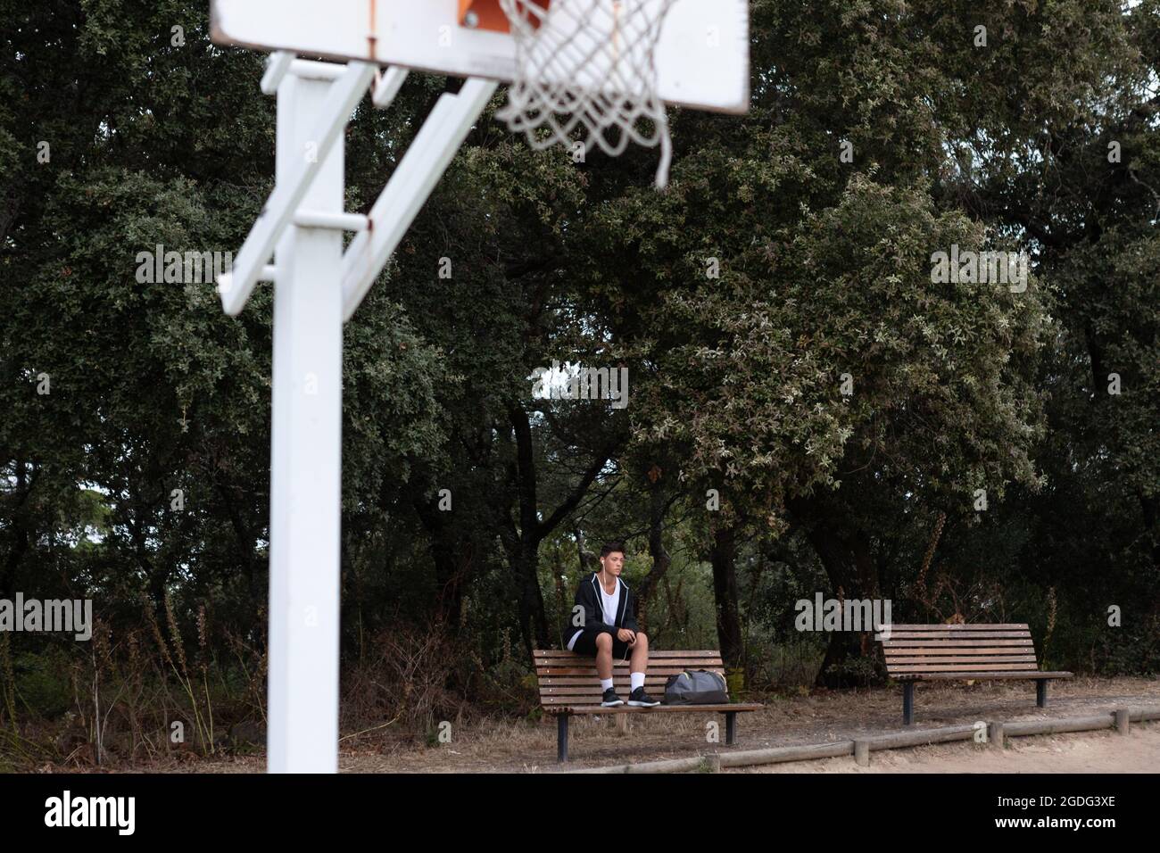 Male teenage basketball player sitting on park bench by basketball ...
