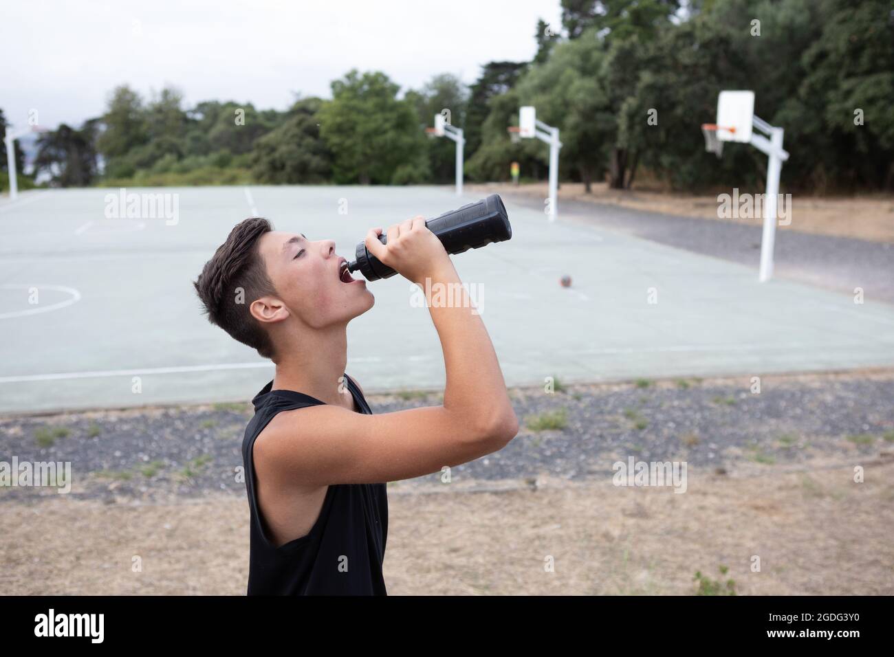 Male teenage basketball player drinking from water bottle on basketball ...