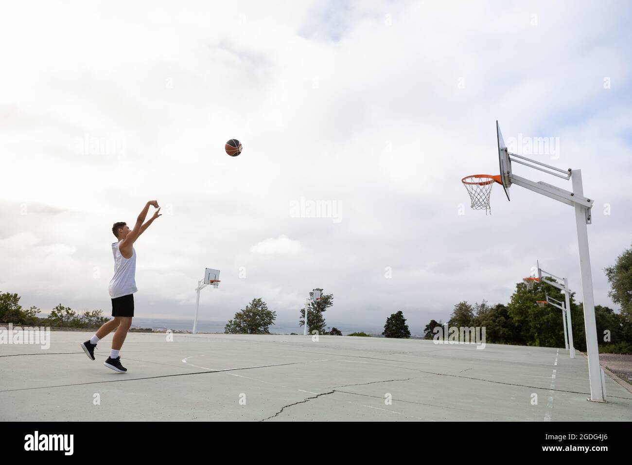 Male teenage basketball player throwing ball toward basketball hoop ...