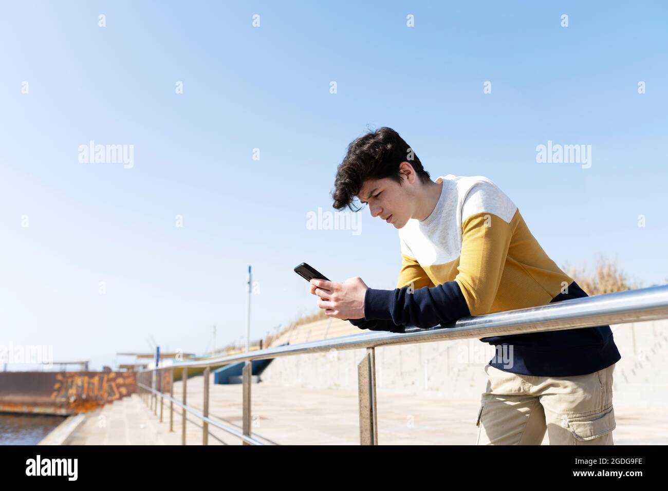 Young man using a smart phone texting messages , leaning on railing ...