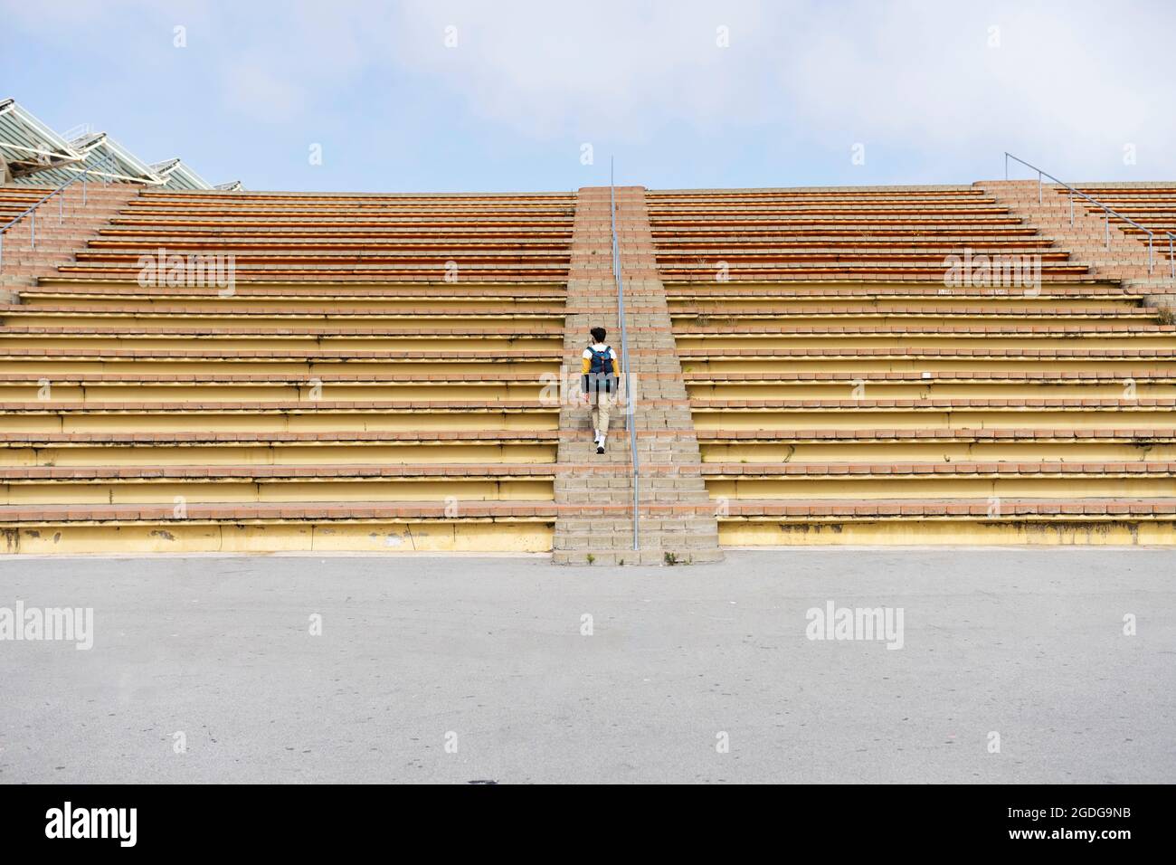 Rear view of a young student with backpack going up stairs of bleacher ...