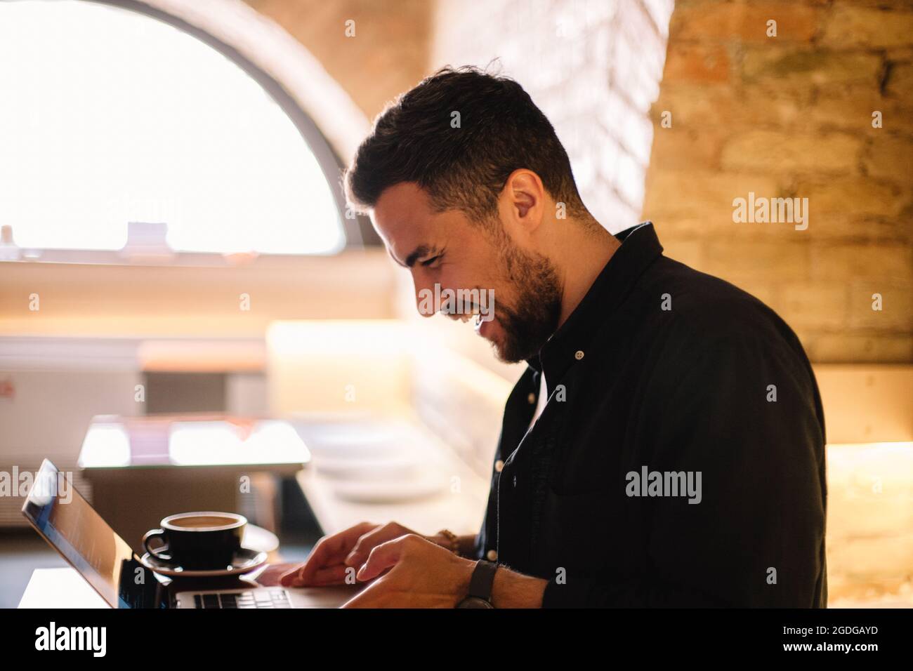 Happy man laughing while using laptop computer at cafe Stock Photo - Alamy